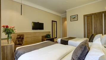 Quarto de hotel com duas camas, televisão, espelho e cabeceira de madeira.