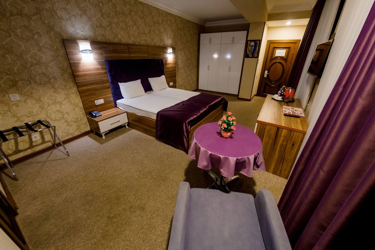 Quarto de hotel com cama, mesa de cabeceira, cadeira e uma pequena mesa com um vaso de flores.