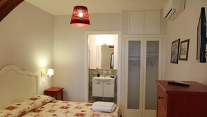 Quarto com cama, mesa de cabeceira, guarda-roupa e banheiro visível através de uma porta aberta.