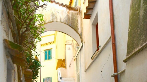 Uma escadaria de pedra estreita conduz a um edifício com fachada amarela e um arco branco.