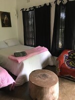 Quarto com duas camas, um banquinho de madeira e uma cadeira colorida.