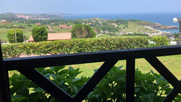 Paisagem costeira com casas, vegetação e vista clara do mar.