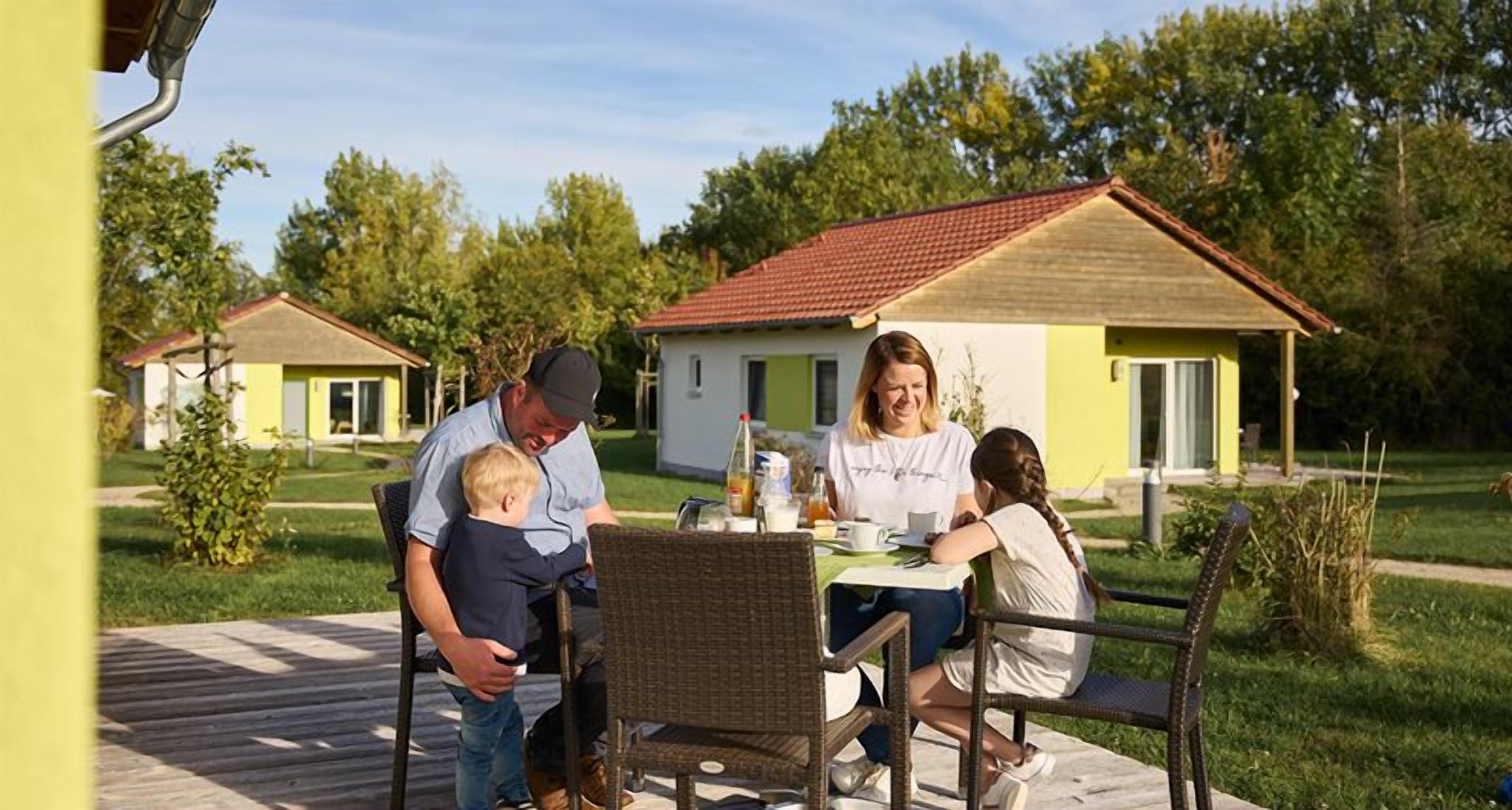 Uma família jantando ao ar livre em um terraço com vista para casas e vegetação.
