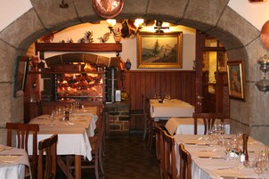 Um restaurante com arcos de pedra, mesas de madeira e lareira de pedra.