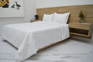 Quarto moderno com cabeceira de madeira, roupa de cama branca, mesa de cabeceira com um vaso de flores e um quadro na parede.