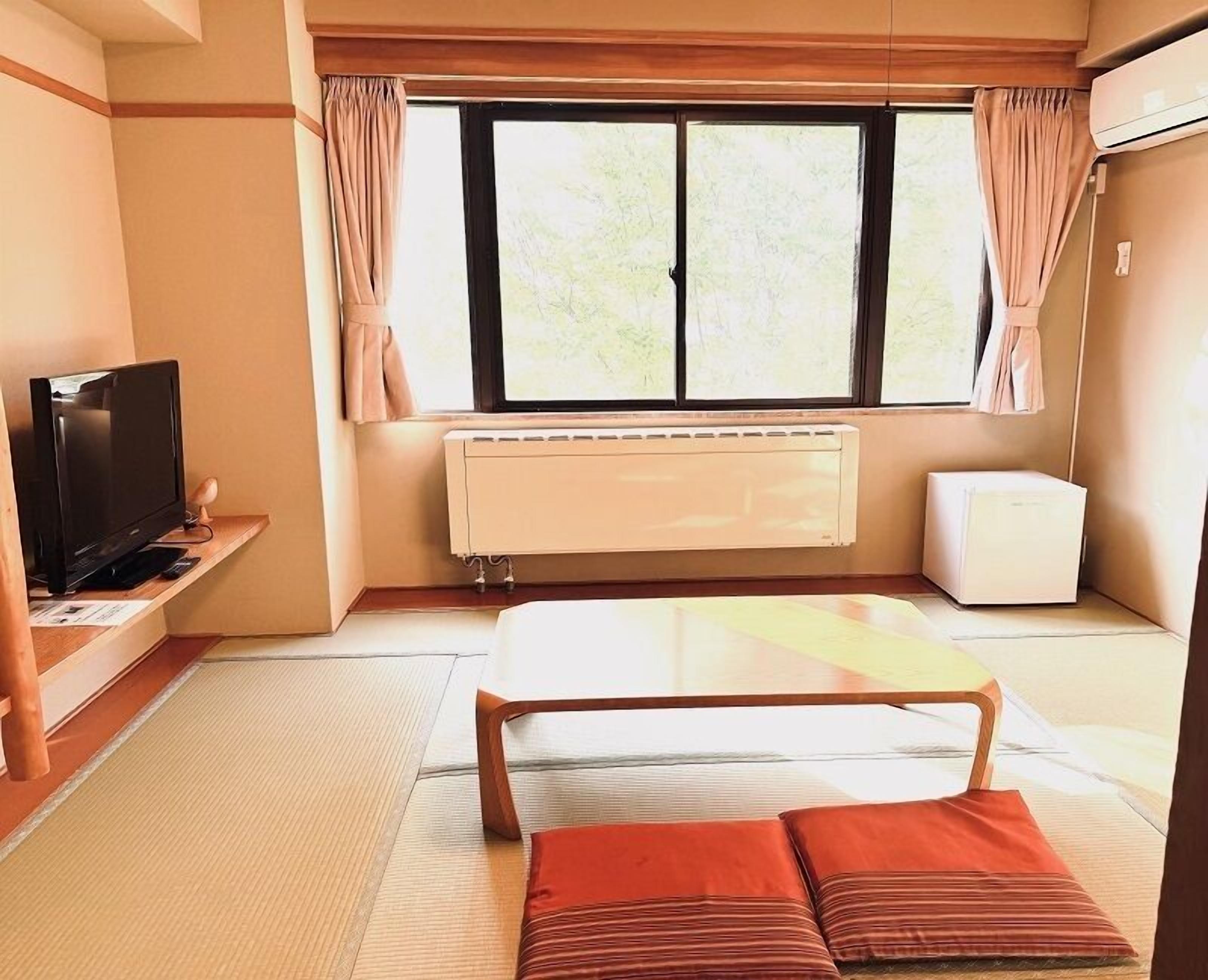 Quarto com cama, televisão, radiador e janela com cortinas.