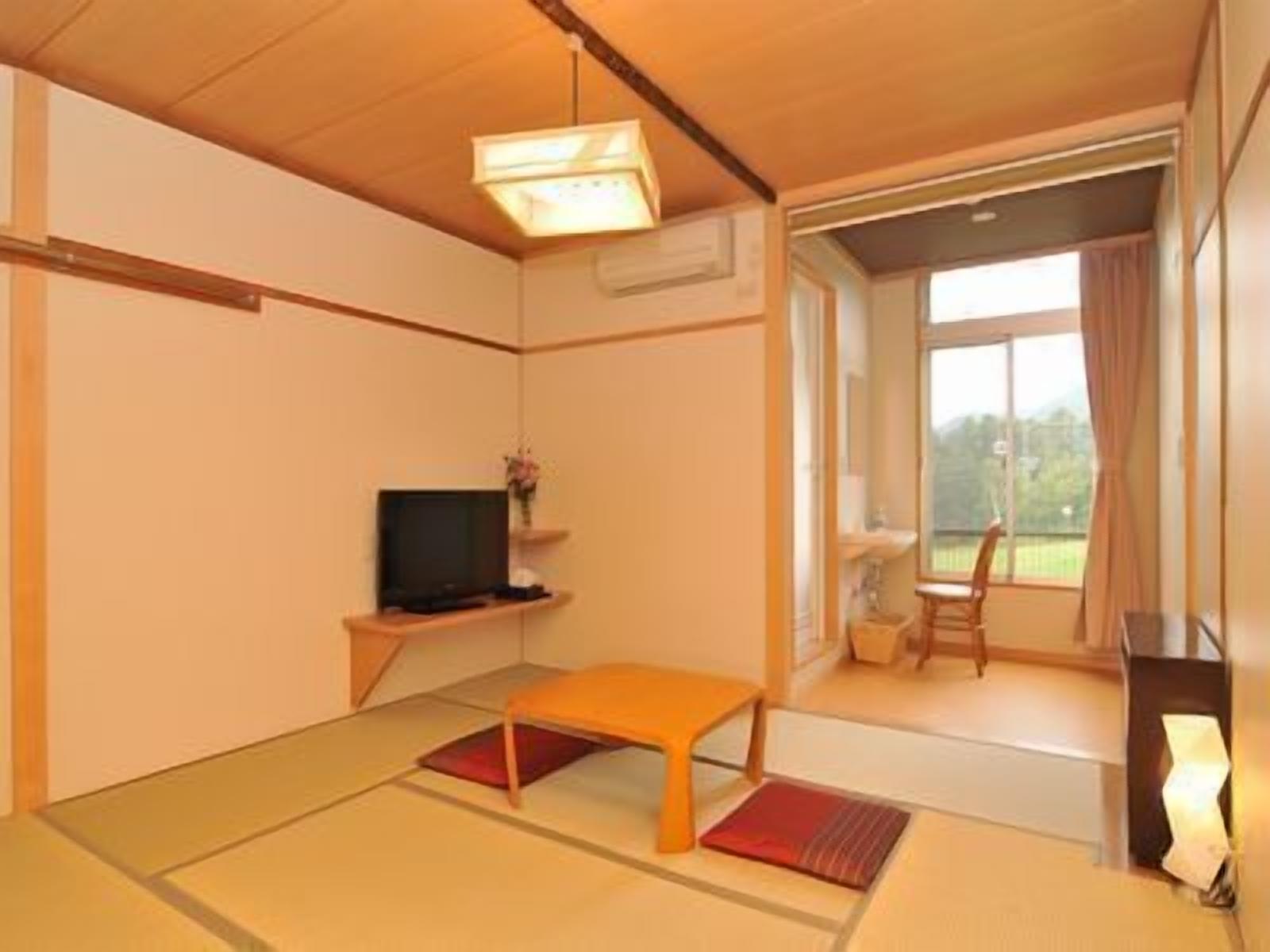 Quarto com tatames, televisão, uma mesinha e janela com cortinas.