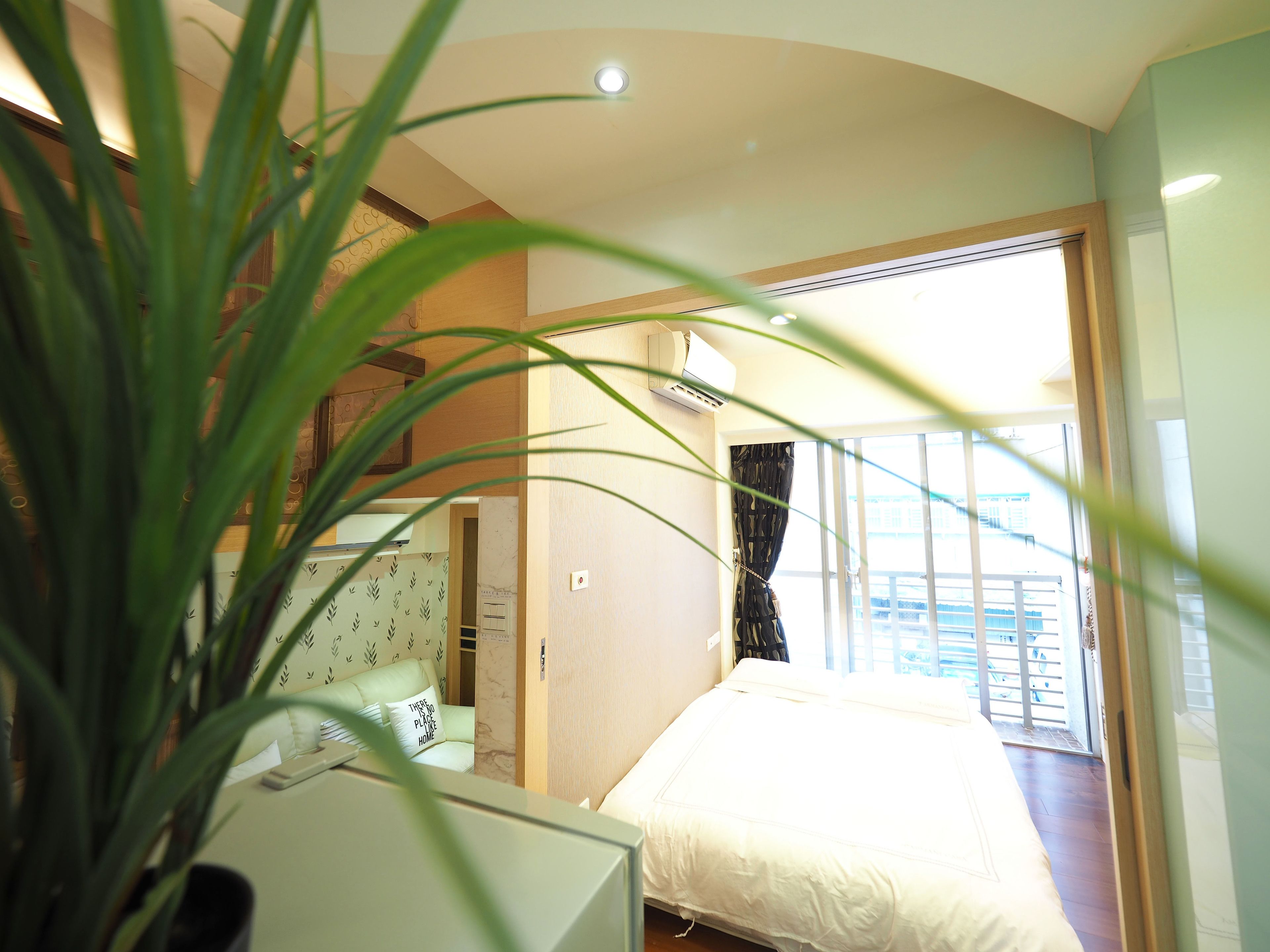 Um quarto com uma cama, um vaso de planta, uma janela com cortinas e um ar condicionado.