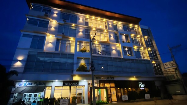Um hotel de vários andares com janelas e varandas iluminadas, um letreiro com 'One Fish' no andar térreo e 'Rolle De Luxe & Labo Center' no segundo andar.