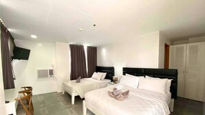 Quarto de hotel com duas camas, uma escrivaninha, uma cadeira, uma televisão e um guarda-roupa.