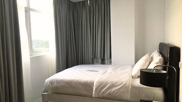 Quarto de hotel com cama, mesa de cabeceira, luminária e janela com cortinas.