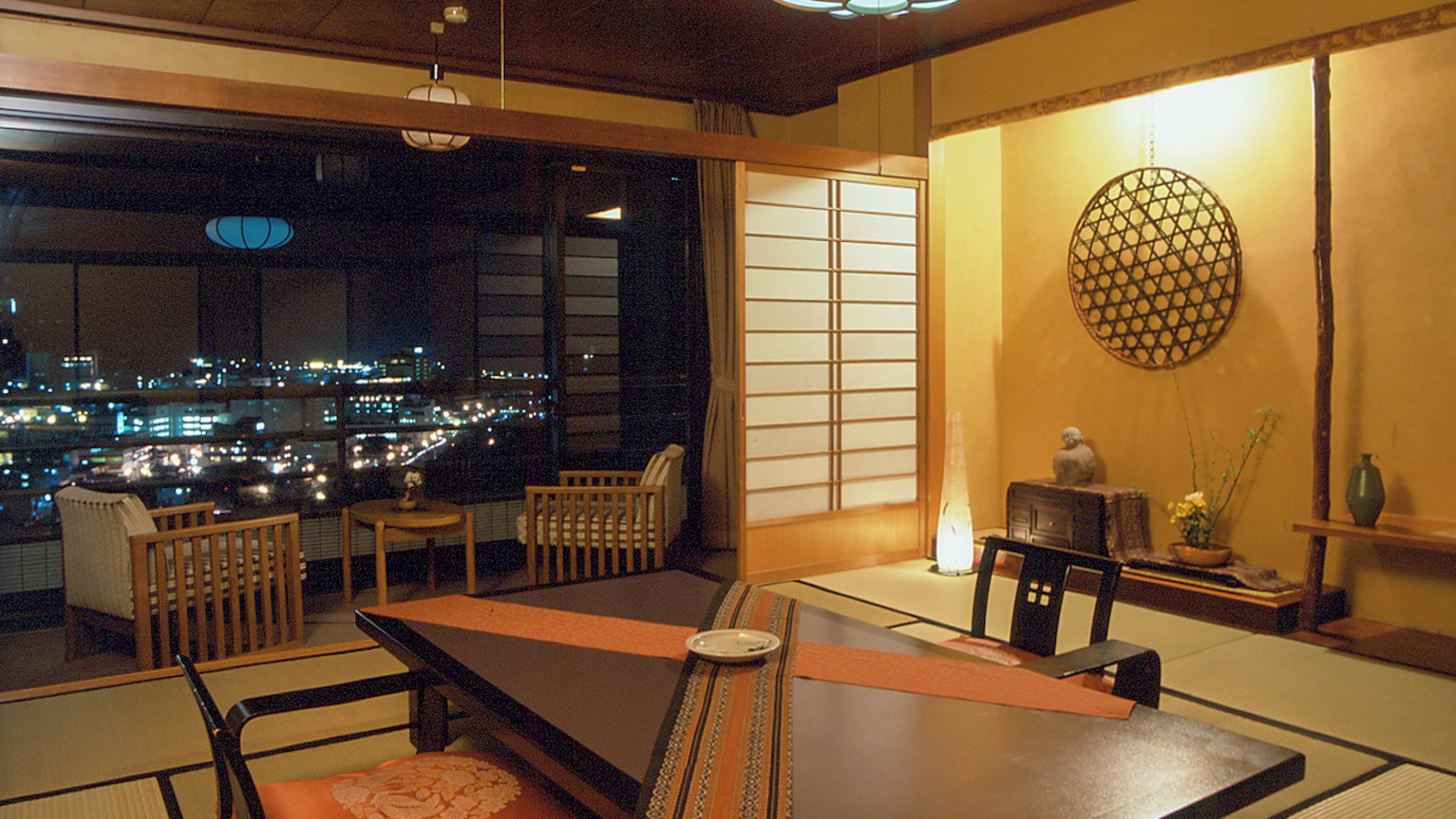 Um quarto japonês tradicional com tatame, uma mesa baixa e vista para o horizonte noturno.