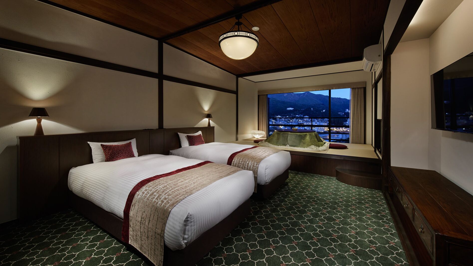 Quarto de hotel com duas camas, vista para a cidade, uma janela grande e teto de madeira.