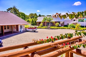 Um hotel com calçada de acesso, um carro vermelho estacionado em frente e uma cerca de madeira com flores vermelhas.