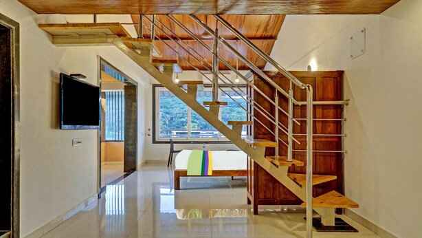 Um interior moderno com escada de madeira, cama com manta colorida e uma grande janela com vista para árvores.