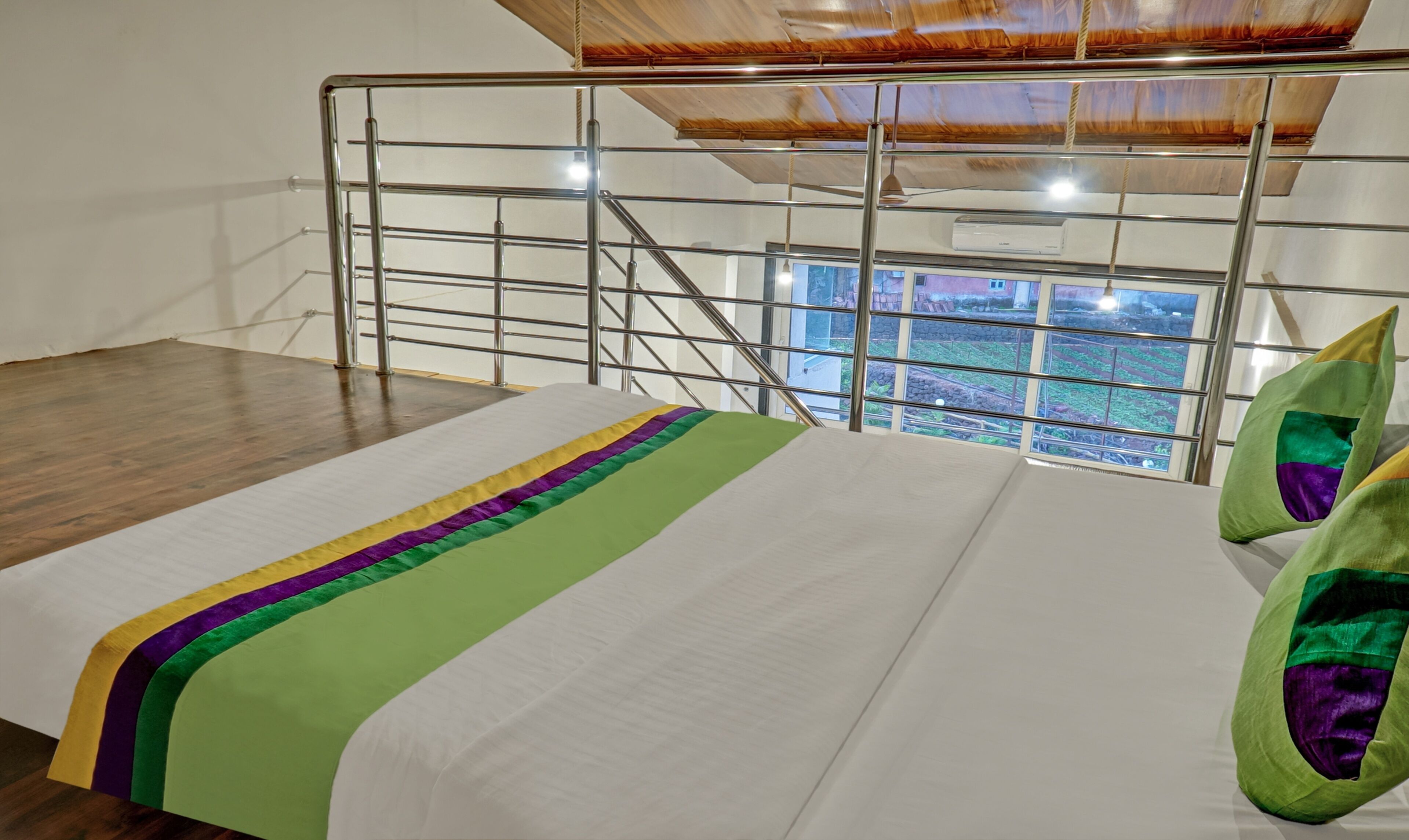 Quarto com uma cama, vista de um jardim pela janela e escada de metal.