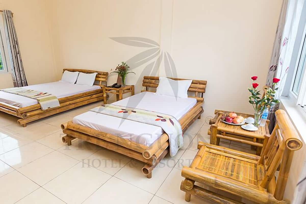 Quarto de hotel com duas camas de madeira, uma mesa pequena de madeira com bandeja e uma janela com cortinas.