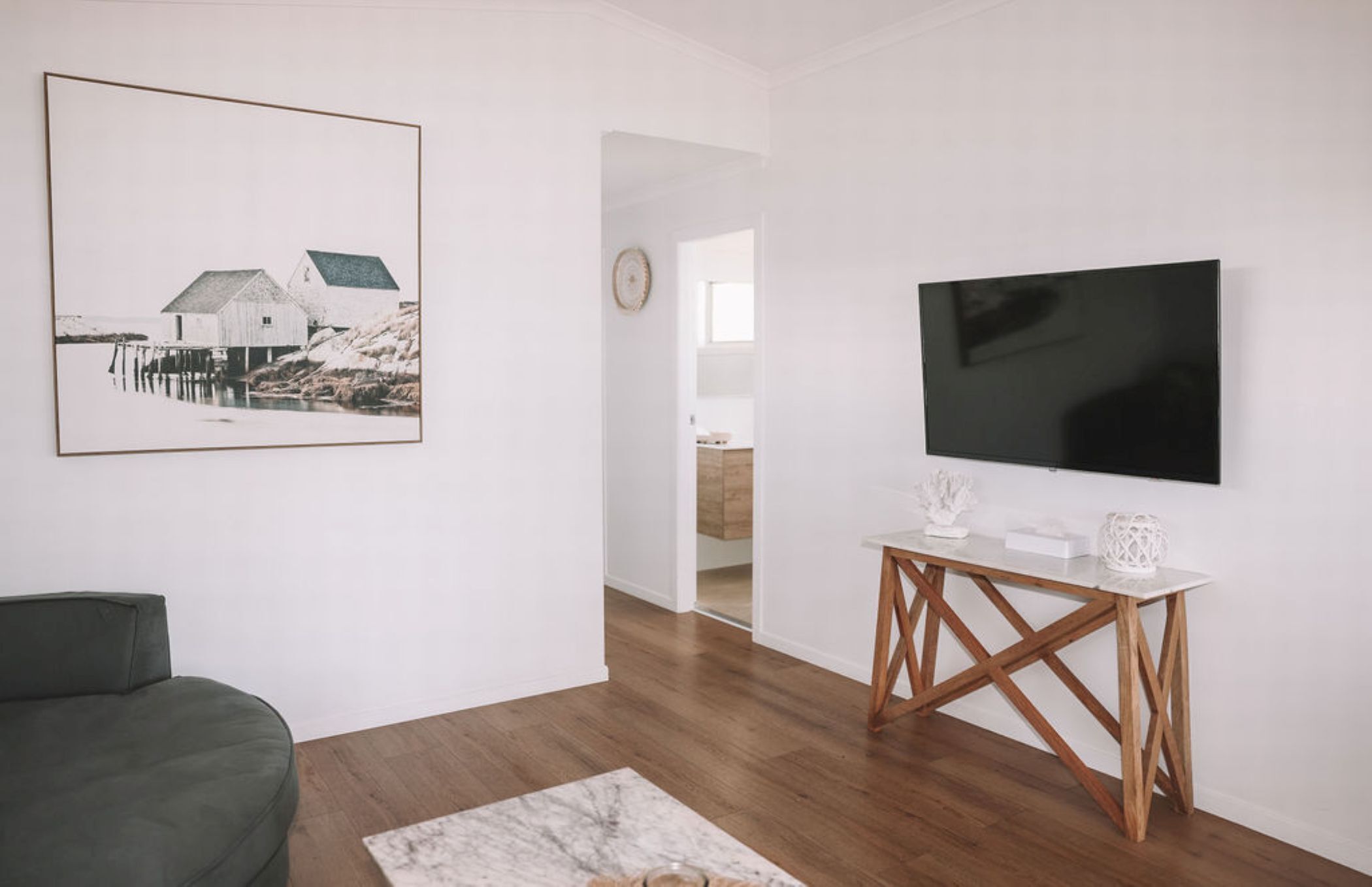 Uma sala de estar minimalista com um sofá verde, uma mesa de centro de madeira e uma grande TV de tela plana na parede.