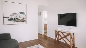 Uma sala de estar minimalista com um sofá verde, uma mesa de centro de madeira e uma grande TV de tela plana na parede.