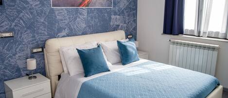 Quarto com cama, mesa de cabeceira, abajur e um quadro na parede.