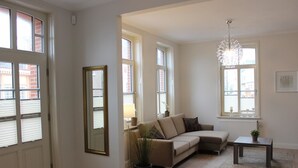 Uma sala de estar com um sofá bege, uma mesa pequena, um vaso de planta e um candelabro.