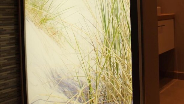 Quadro com uma paisagem de praia, mostrando areia e grama, visto através de uma janela.