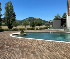 Piscina com deck de madeira, cercada por árvores e vista para uma montanha.