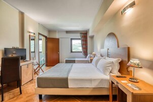 Quarto de hotel com cama, escrivaninha, televisão e janela com cortinas.