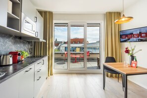 Cozinha moderna com área de jantar, vista do horizonte urbano através de uma porta de vidro e uma mesa com um vaso de flores.
