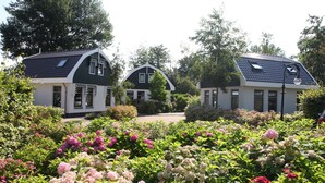 Um edifício residencial com projeto simétrico, apresentando um arco central e um jardim com diversas plantas floridas.