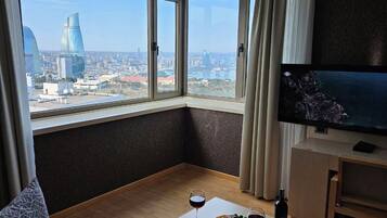 Quarto de hotel moderno com uma janela grande que oferece vista para a cidade, uma mesa de jantar posta para dois e uma TV de tela plana em um suporte.