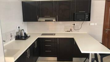 Cozinha moderna com armários escuros, bancada branca e micro-ondas embutido.