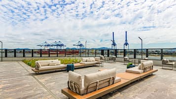 Um terraço com área de estar ao ar livre, vista para o porto e guindastes ao fundo.