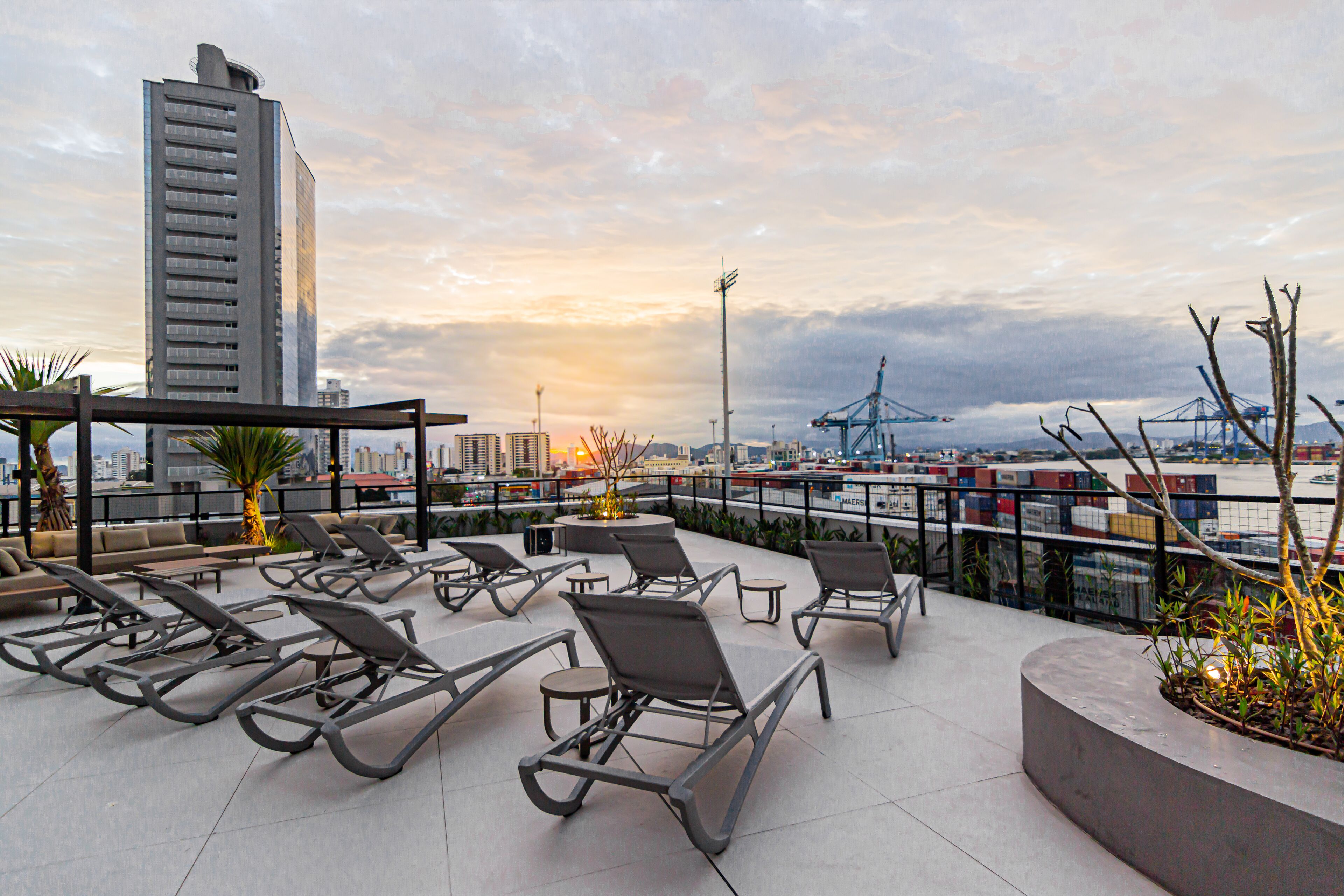 Terraço no telhado com espreguiçadeiras, uma mesinha e um vaso de planta.