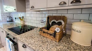 Cozinha com armários brancos, bancada de granito, chaleira, cesta com pão e recipiente para pão.