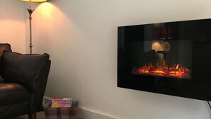 Uma sala de estar com uma televisão de tela plana na parede, um sofá de couro, um abajur e uma pequena cesta com uma caixa.