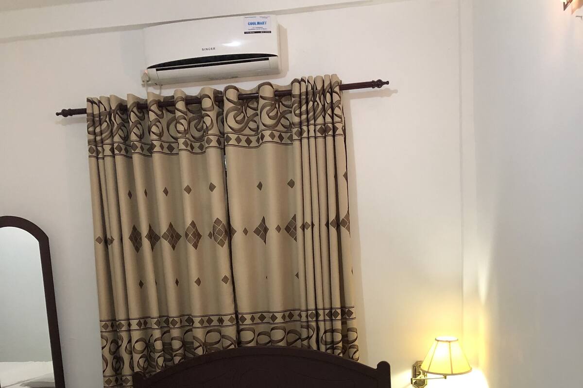 Quarto com cama, mesa de cabeceira, espelho, ar condicionado fixado na parede e luminária.