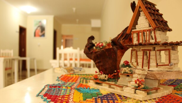 Uma mesa com um tapete tecido colorido, uma escultura de cavalo de madeira e um pequeno modelo de casa.
