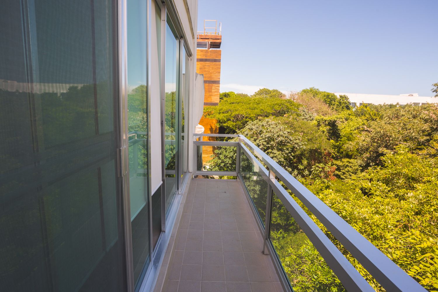 Um edifício moderno com grandes janelas e uma varanda com vista para uma paisagem verdejante.
