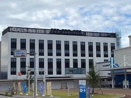 Edifício moderno com fachada branca e várias janelas. Sinalização indica área de construção nova.