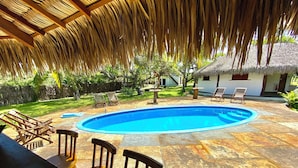 Piscina com espreguiçadeiras e uma cobertura de palha.