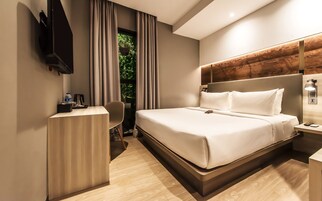 Quarto de hotel moderno com uma cama grande, uma escrivaninha, uma cadeira e uma televisão.