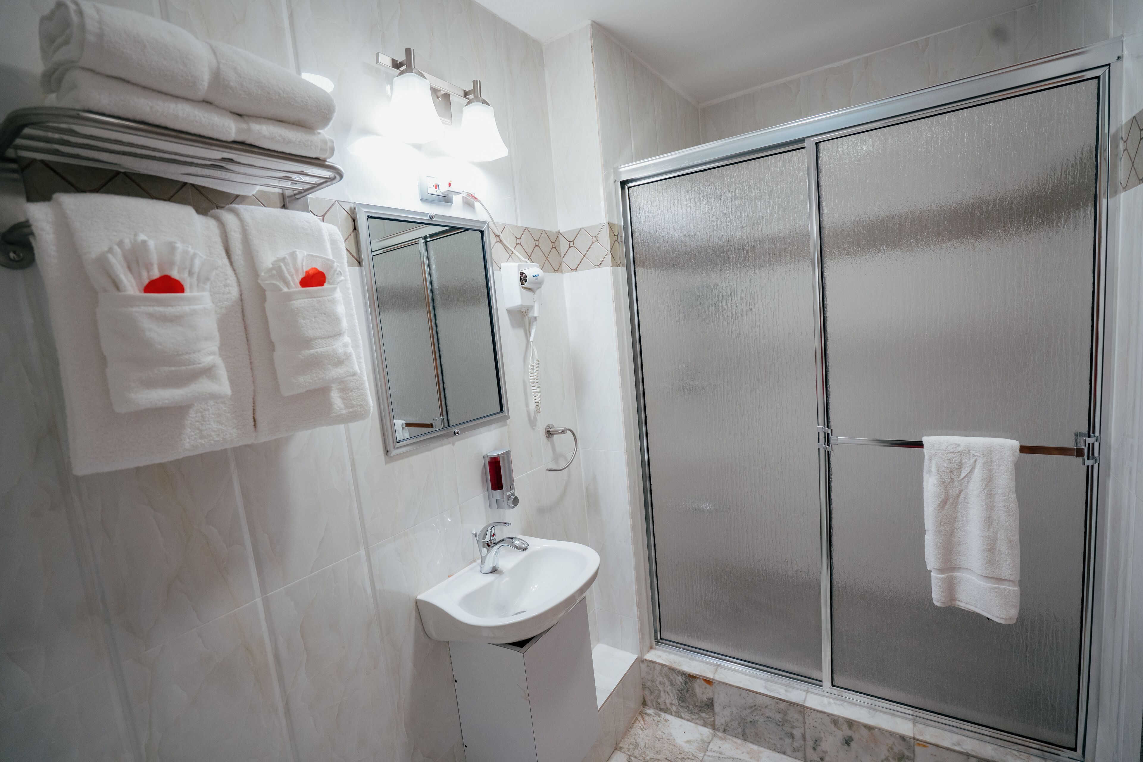 Uma casa de banho moderna com cabine de duche em vidro, lavatório branco e toalheiro com toalhas dobradas.