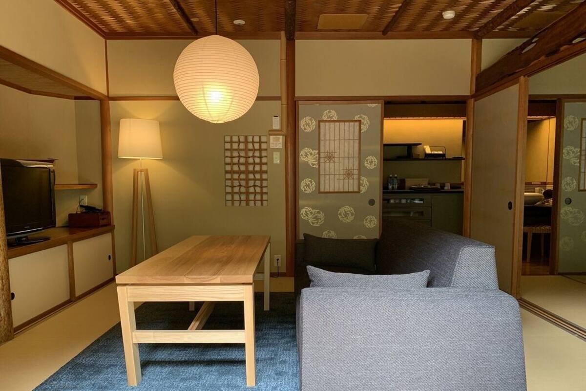 Um quarto japonês tradicional com tatames, uma mesa de madeira baixa, um sofá, um lanterna de papel pendurada e portas deslizantes.