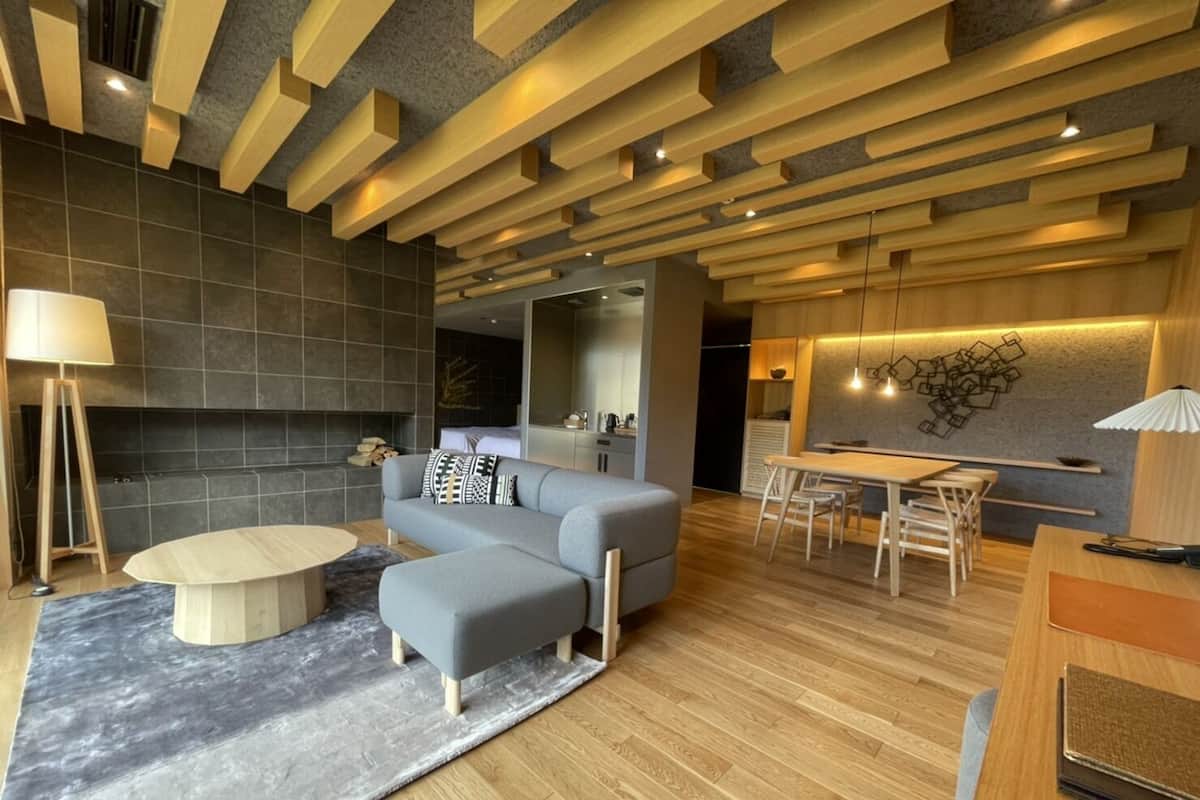 Uma sala de estar moderna com um sofá, um banquinho e uma mesa de centro redonda, uma lareira e um espaço de refeições com mesa e cadeiras.