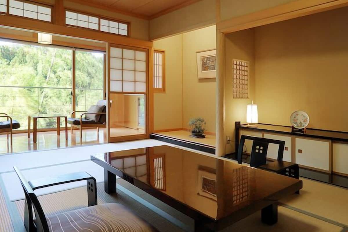 Um quarto japonês tradicional com tatames, uma mesa baixa, almofadas e portas deslizantes.