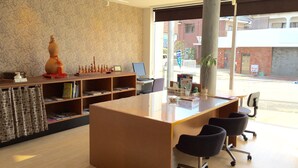 Uma área de recepção com uma mesa de madeira, duas cadeiras de escritório pretas, um computador e uma estante com objetos decorativos.