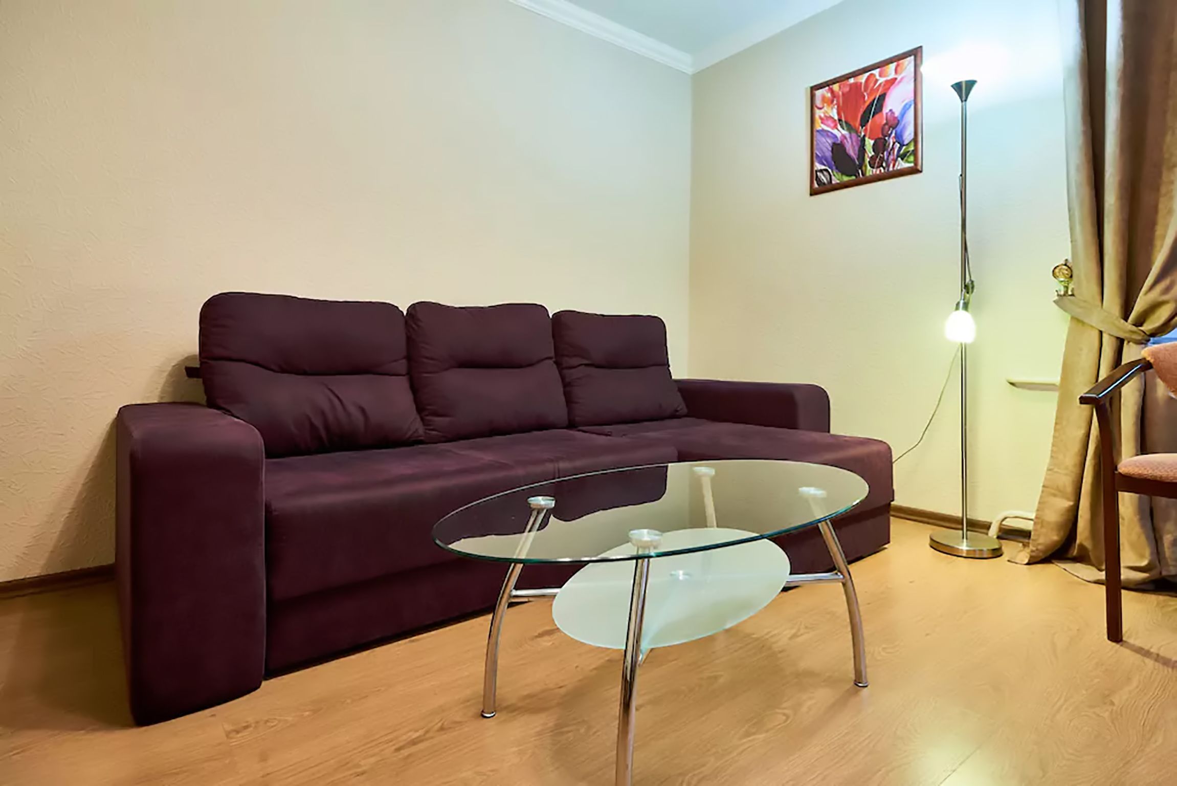 Uma sala de estar com um sofá roxo, uma mesa de centro de vidro e um abajur.