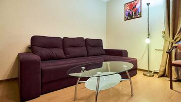 Uma sala de estar com um sofá roxo, uma mesa de centro de vidro e um abajur.