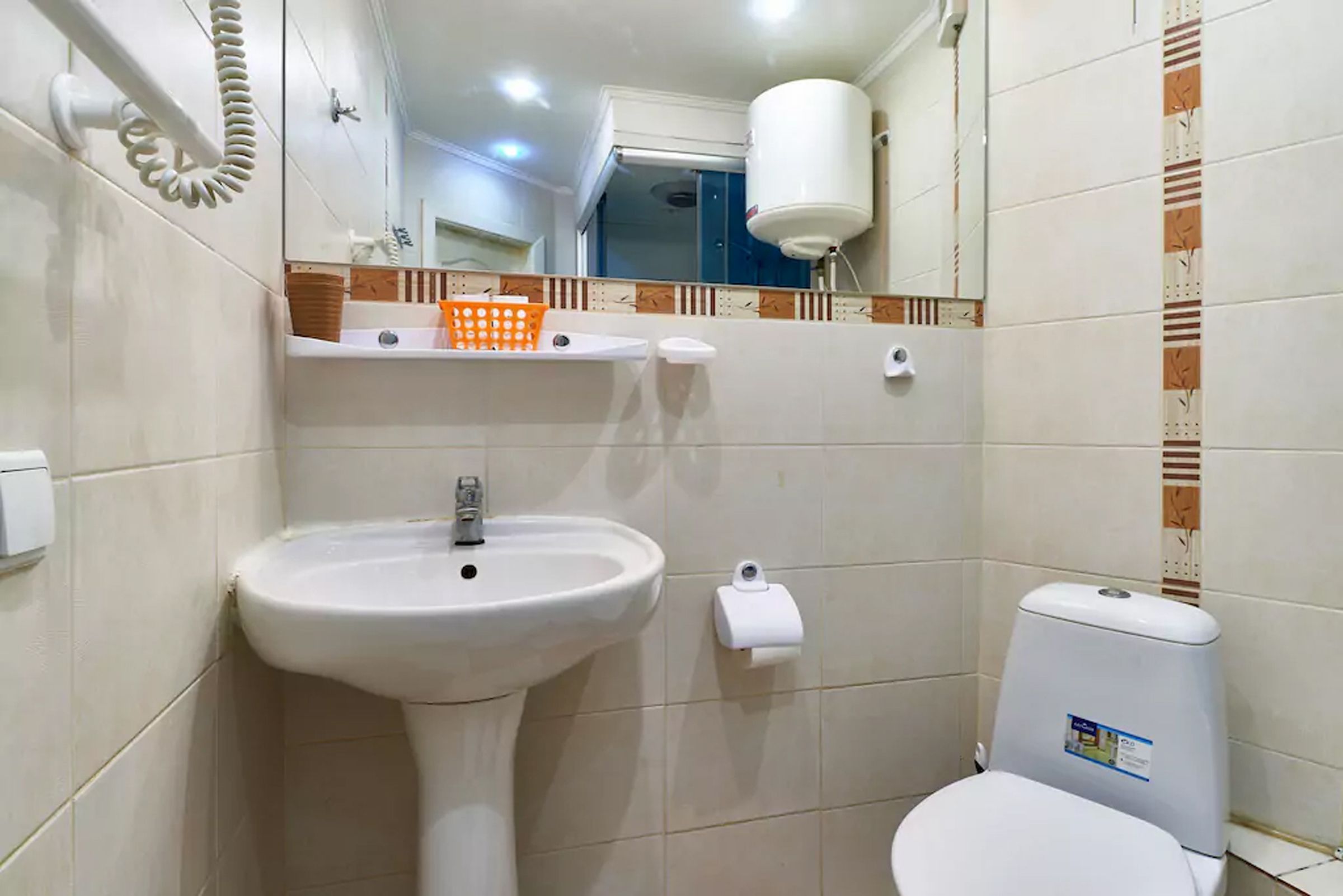 Casa de banho com lavatório branco, sanita e espelho sobre o lavatório.